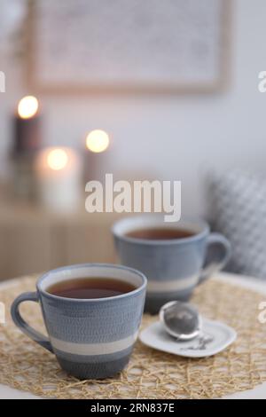 Cups of tea and snap infuser with dry leaves on white coffee table ...