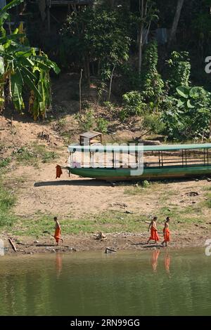 Young buddhist monk taking bath in the river near a boat in Luang ...