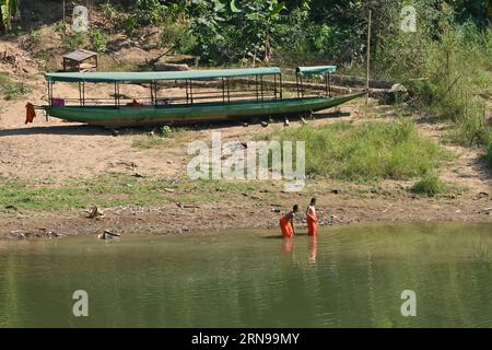 Young buddhist monk taking bath in the river near a boat in Luang ...
