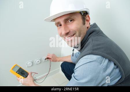 electrician checking voltage in a partially installed electrical wall ...