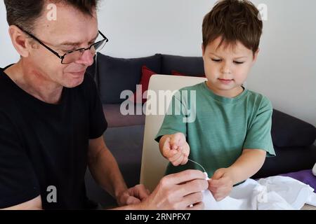 Father teaching his son how to sew on a button. Shot at home Stock ...