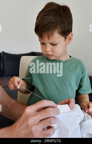 Father teaching his son how to sew on a button. Shot at home Stock ...