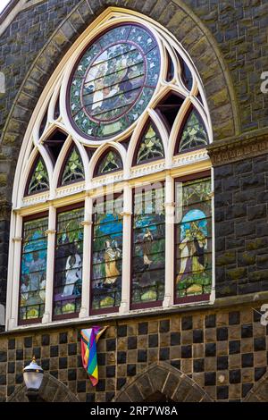 Pride flag hanging below a stained glass window on the front of a ...