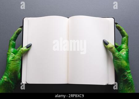 Green monster hands holding notebook with copy space on grey background ...