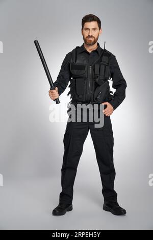 Handsome dark-haired police officer carrying baton on shoulder in ...
