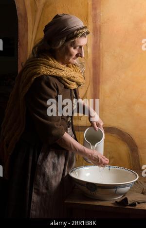 Woman in peasant renaissance costume washing her hands in an antique ...