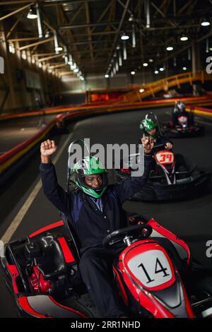 excited african american go cart racer in helmet raising hands and ...
