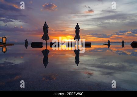 Closed umbrellas reflecting in an infinity pool overlooking the sea in ...