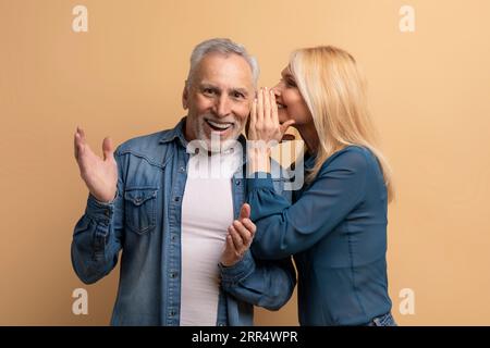 Mature woman sharing secret with her husband, beige background Stock ...
