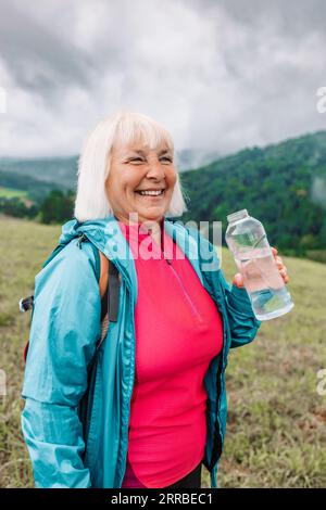 caucasian 50s blonde girl drinking water from plastic bottle. Mountain ...