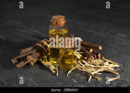 Dried sticks of licorice root and bottles with essential oil on black ...