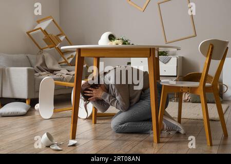 Young woman hiding under dining table during earthquake at home Stock ...