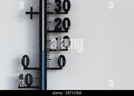 Classic black analog thermometer hanging on white wall displaying blue ...