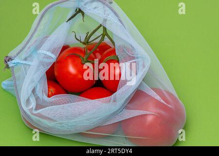 Shopping green mesh bag with tomatoes on white table. Zero waste ...