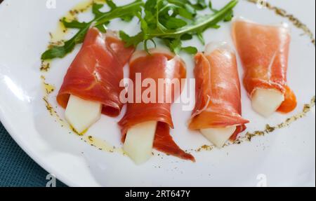 Rolls of iberian jamon stuffed with melon at plate with arugula ...