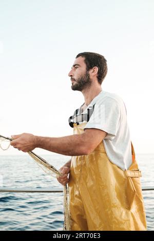 Focused bearded male fisher in uniform seiner hunting fish with net ...
