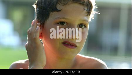 Boy scratching ear casually outside. Portrait of kid scratches body ...