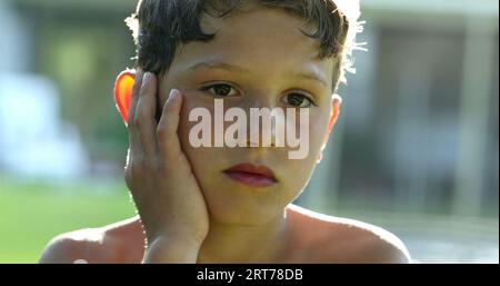 Boy scratching ear casually outside. Portrait of kid scratches body ...
