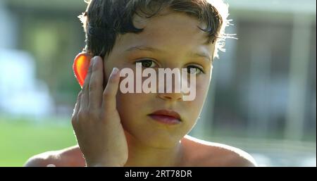 Boy scratching ear casually outside. Portrait of kid scratches body ...