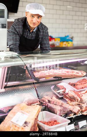 Diligent male butcher offering to sell big piece of beef beef in ...