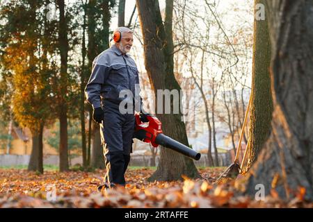 Focused male gardener in uniform taking photos of flowers and potted ...