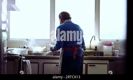 Back of senior chef preparing meal at home by kitchen sink. Retired ...