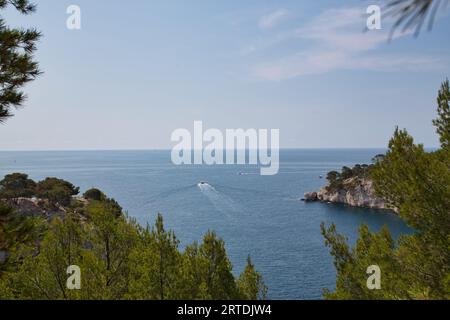A boat in a calanque, green cliffs and red contrast. Blue water and sky ...