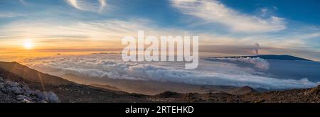 Spectacular scene of the golden twilight above the clouds at Mauna Kea with view of the smoke ...
