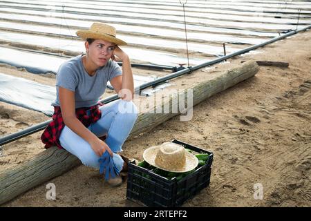 Tired farm worker sits on log after covering plants with covering ...