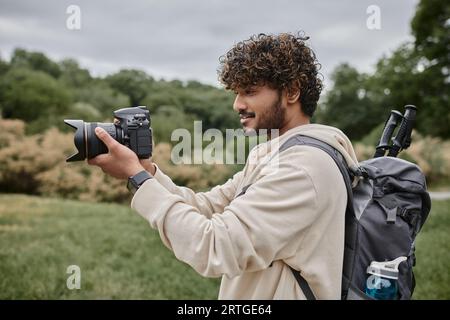 curly indian photographer with backpack taking photo on professional ...