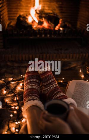 Faceless woman sitting by fireplace and holding mug Stock Photo - Alamy