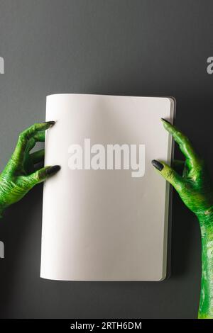 Vertical image of green monster hands holding notebook with copy space ...