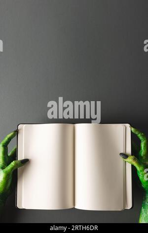 Vertical image of green monster hands holding notebook with copy space ...
