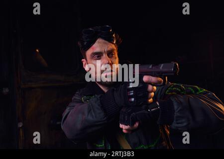 unshaven man with military googles aiming with gun in abandoned subway ...