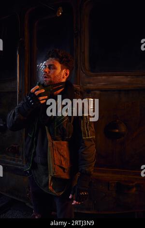 man in worn clothes and gas mask looking at camera in abandoned post ...