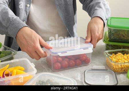 Man closing plastic container with lid at light grey marble table in ...