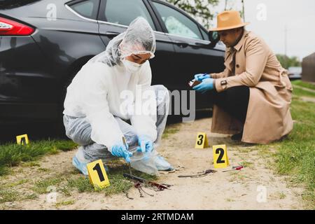 Investigator and criminologist working with evidences at crime scene near car outdoors Stock ...