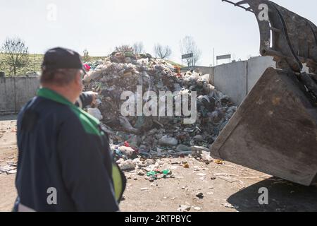 Landfill worker directing skid steer loader on the garbage heap. Waste ...