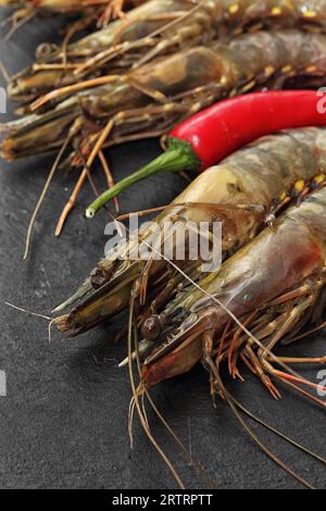 Raw unpeeled king prawns with a red chilli pepper on black slate Stock Photo - Alamy