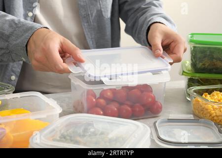 Man closing plastic container with lid at light grey marble table in ...