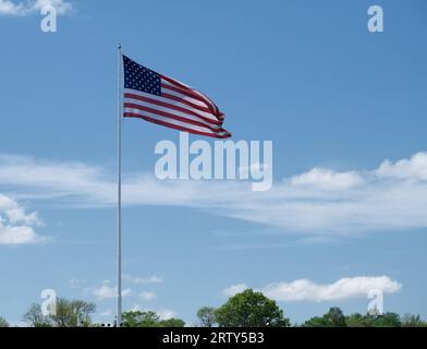 Large United States flag on a tall flagpole against a blue sky with ...