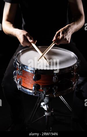 A man plays a musical percussion instrument with sticks on a dark ...