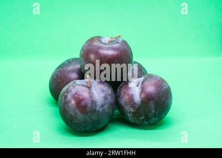 Ripe plums against a green background, with a bite taken from one Stock ...