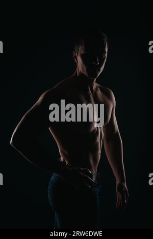 Stunning and well-built man standing in a dark room and flexing his ...
