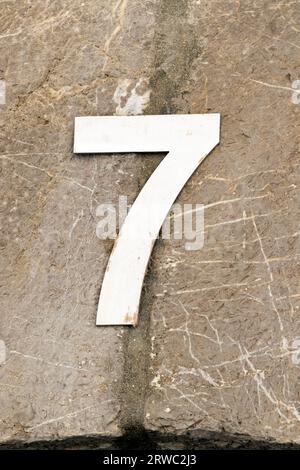 White number Seven house number on a blue metalic plate on a stone wall ...