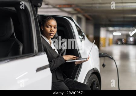 Professional operating computer in EV on charge in garage Stock Photo ...