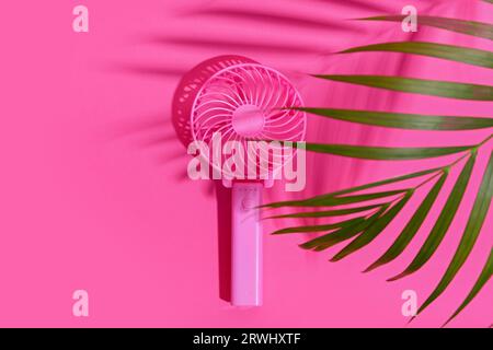 Portable electric fan and palm leaf on pink background with space for ...
