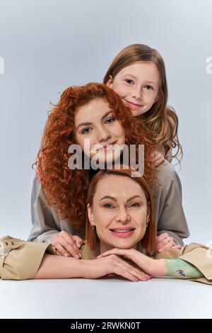 three female generations, happy redhead family in beige coats sitting ...