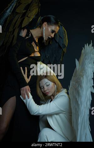 women in Halloween costumes of angel and demon with wings sitting on ...