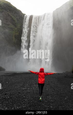 Under the waterfall in iceland with a red coat on Stock Photo - Alamy